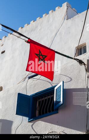 Bright red Moroccan flag with green star on a clear blue sky background ...