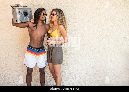 Man in swimsuit hugging bikini clad girlfriend from behind on green ...