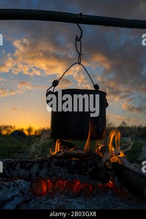 Black pot are heating under fire. Hand holding big wood spoon under pot ...