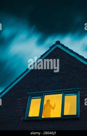 Burglar with pistol in eerie house with illuminated window under stormy ...