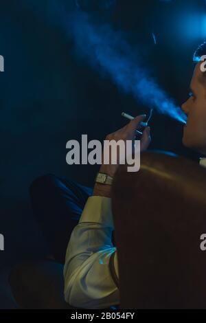 Retro fashion man smokes a cigarette and is sitting in leather armchair ...