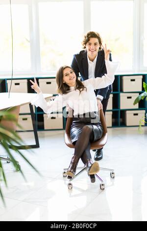 Businesswoman pushing playful colleague in office chair Stock Photo - Alamy