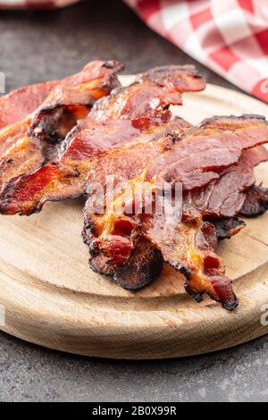 Fried bacon on cutting board. Sliced roasted bacon on old kitchen table ...
