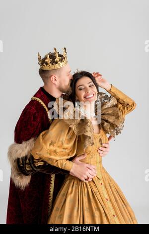 king with crown hugging and kissing attractive queen isolated on grey ...