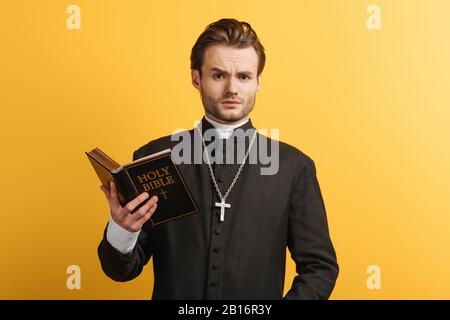 shocked catholic priest reading holy bible isolated on yellow Stock ...