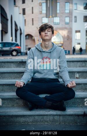 Teenage boy meditating and relaxing in a city park japanese garden ...
