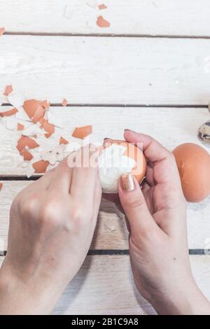 Female hands clean the shell of a boiled egg on a dark wooden ...