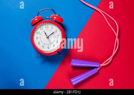 Red alarm clock and jump rope on the color background. Fitness and ...