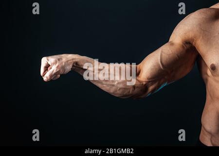 tense arm clenched into fist, veins, bodybuilder muscles on a dark ...