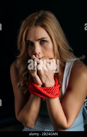 Scared victim with tied hands looking at camera through fingers ...