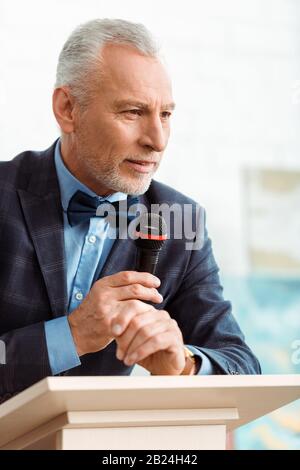 auctioneer in suit talking with microphone and holding gavel during ...