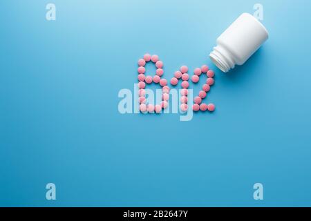 Pink pills in the shape of the letter B12 on a blue background, spilled ...