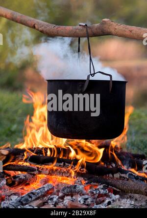 Black pot are heating under fire. Hand holding big wood spoon under pot ...