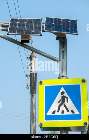 Solar panel with pedestrian crossing lights and sign against blue sky ...