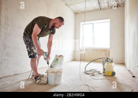 Construction worker mixing mortar in a bucket using handheld concrete ...