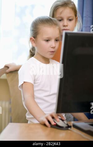 Two girls stand at computer on desk in apartment Stock Photo - Alamy