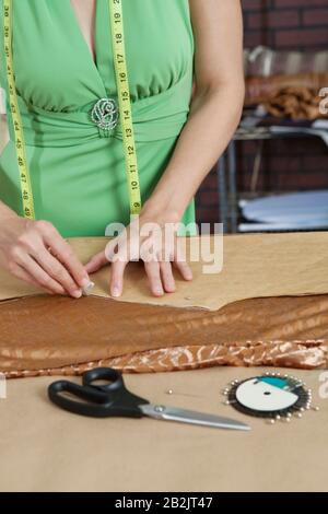 Professional adult female tailor marking cloth pattern with chalk at ...