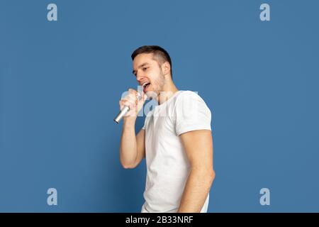 Singing like celebrities, stars. Caucasian young man's portrait on blue ...