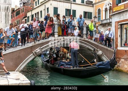 Mass tourism. Crowded bridge over canal, as many tourists watch and ...
