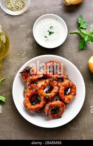 Bacon wrapped onion rings with sauce on plate over dark stone ...