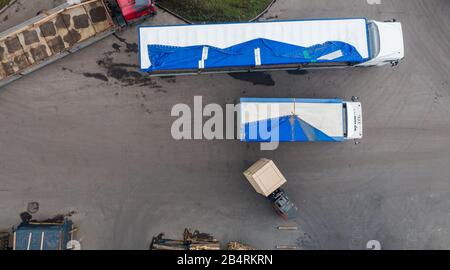 Forklift is putting cargo from warehouse to truck outdoors. Aerial. top ...