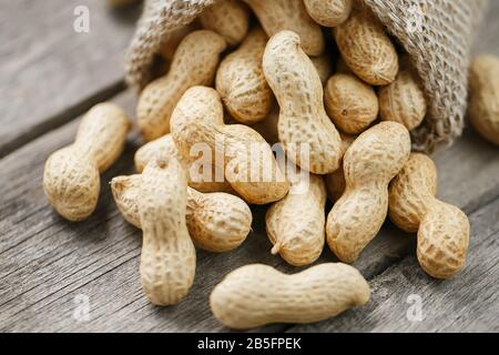 Peanuts in a miniature burlap bag on old, gray wooden surface. Unclean ...