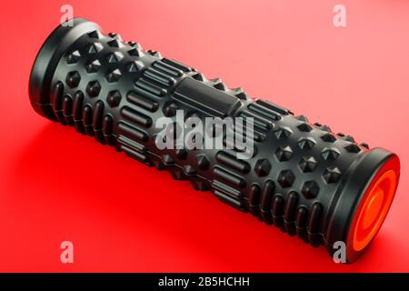 Black lumpy foam massage roller on red background. For the mechanical ...