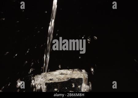 Water jet falling into a glass and generating a splash of water ...