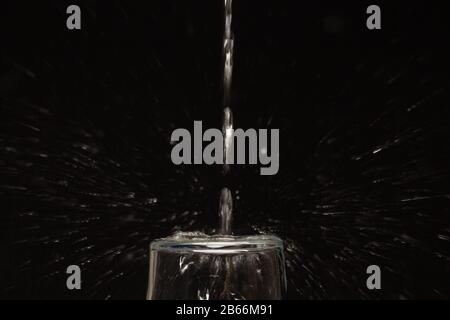 Water jet falling into a glass and generating a splash of water ...