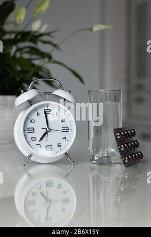 Alarm clock with pills on table in room Stock Photo - Alamy