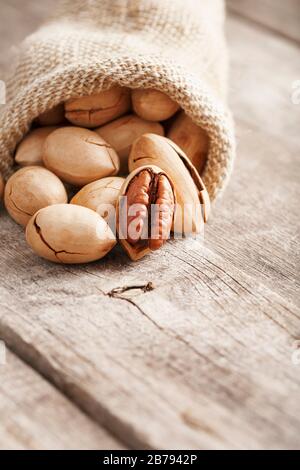 Pecans spill out of a bag on a wooden table, close-up. Peeled, in a ...