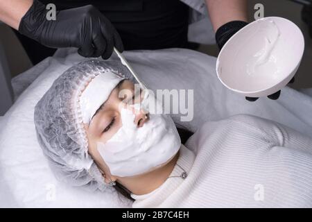 Cosmetologist applies alginate mask with spatula on face of woman ...