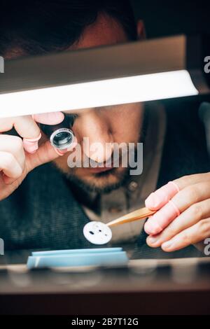 Selective focus of watchmaker holding eyeglass loupe while working at ...
