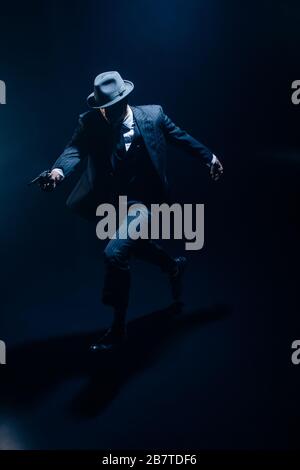 Gangster aiming weapon with outstretched hand on dark background ...