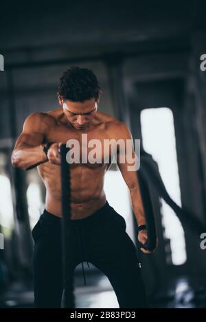 Muscular powerful aggressive man working out with rope in functional ...