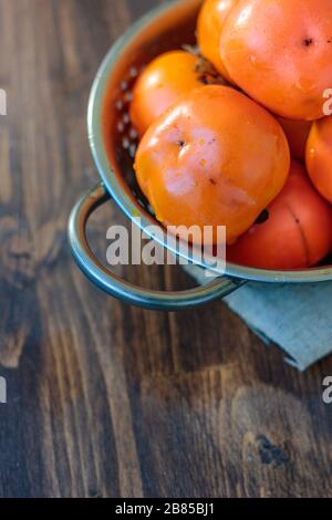 Persimmons in metal collander on wooden table Stock Photo - Alamy