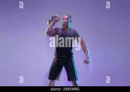 Move. Young african-american bodybuilder training over purple ...