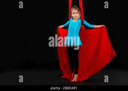 Little acrobat girl shows an acrobatic performance on an aerial hoop ...