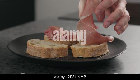 man hand put prosciutto on ciabatta slices black plate Stock Photo - Alamy