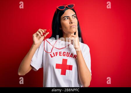 Beautiful lifeguard woman wearing t-shirt with red cross using whistle ...