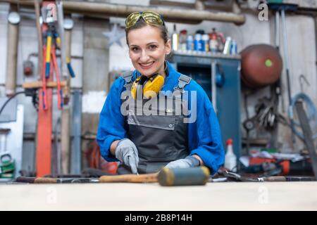 Woman worker marking workpiece in her workshop looking into camera ...