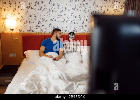 Man and human skeleton watching TV in the bed Stock Photo - Alamy