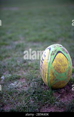 A dirty used full sized Gilbert rugby ball is placed on end in muddy ...
