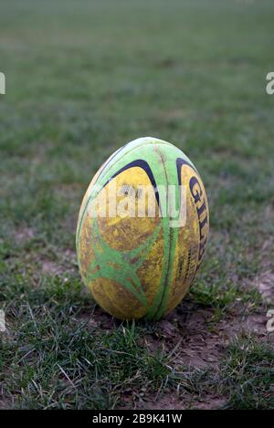 A dirty used full sized Gilbert rugby ball is placed on end in muddy ...