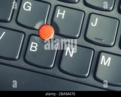 Red trackpoint on a laptop keyboard. A pointing stick is a small ...