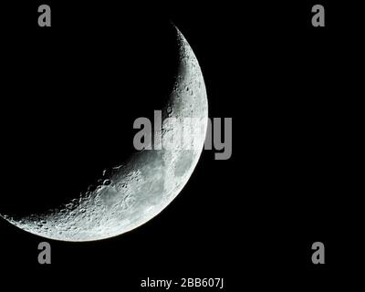 the increasing sickle-shaped quarter moon with its moon craters stands ...