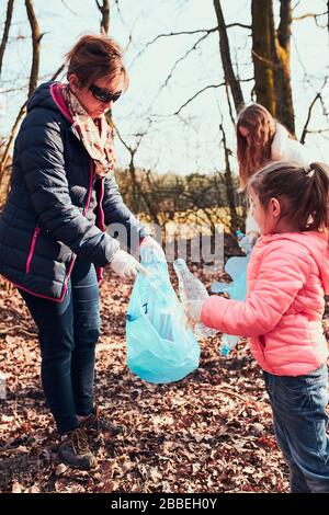 Family cleaning up a forest. Volunteers picking plastic waste to bags ...
