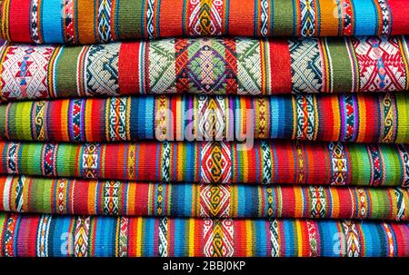 A stack of colorful and traditional Andean textiles on sale in a market ...