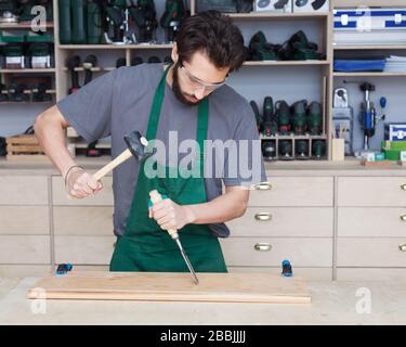 Carpenter in an apron planing a wooden board with a planer, workplace ...