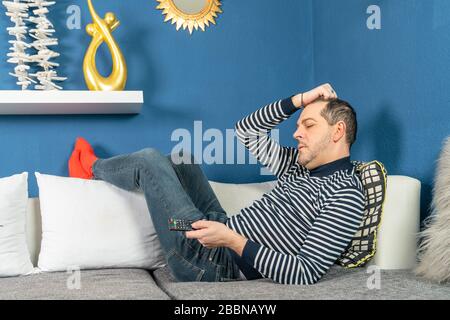 A bored caucasian man lies on the bed and reads a book. Home interior ...